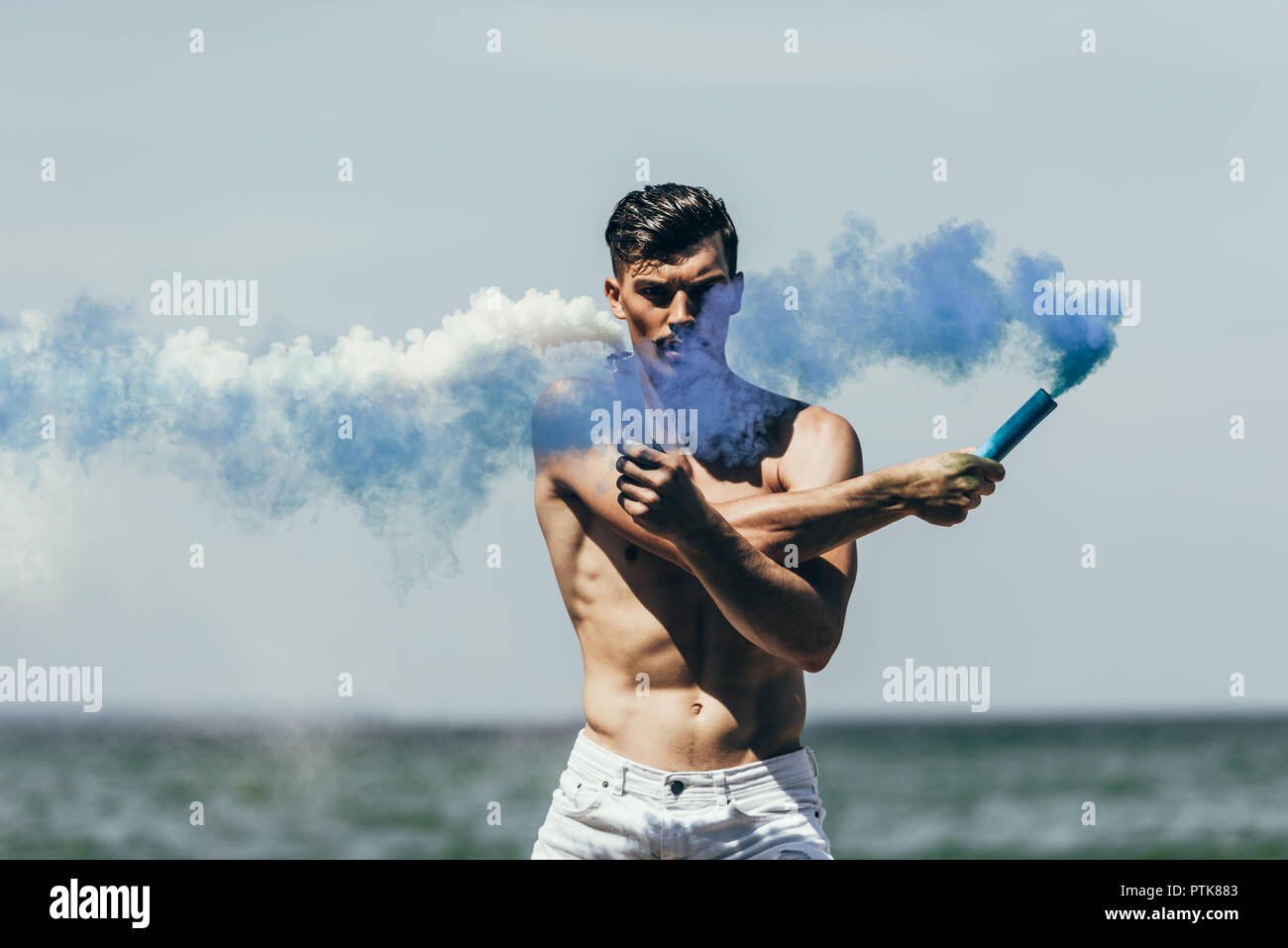 muscular shirtless man with blue and white smoke sticks in front of ...