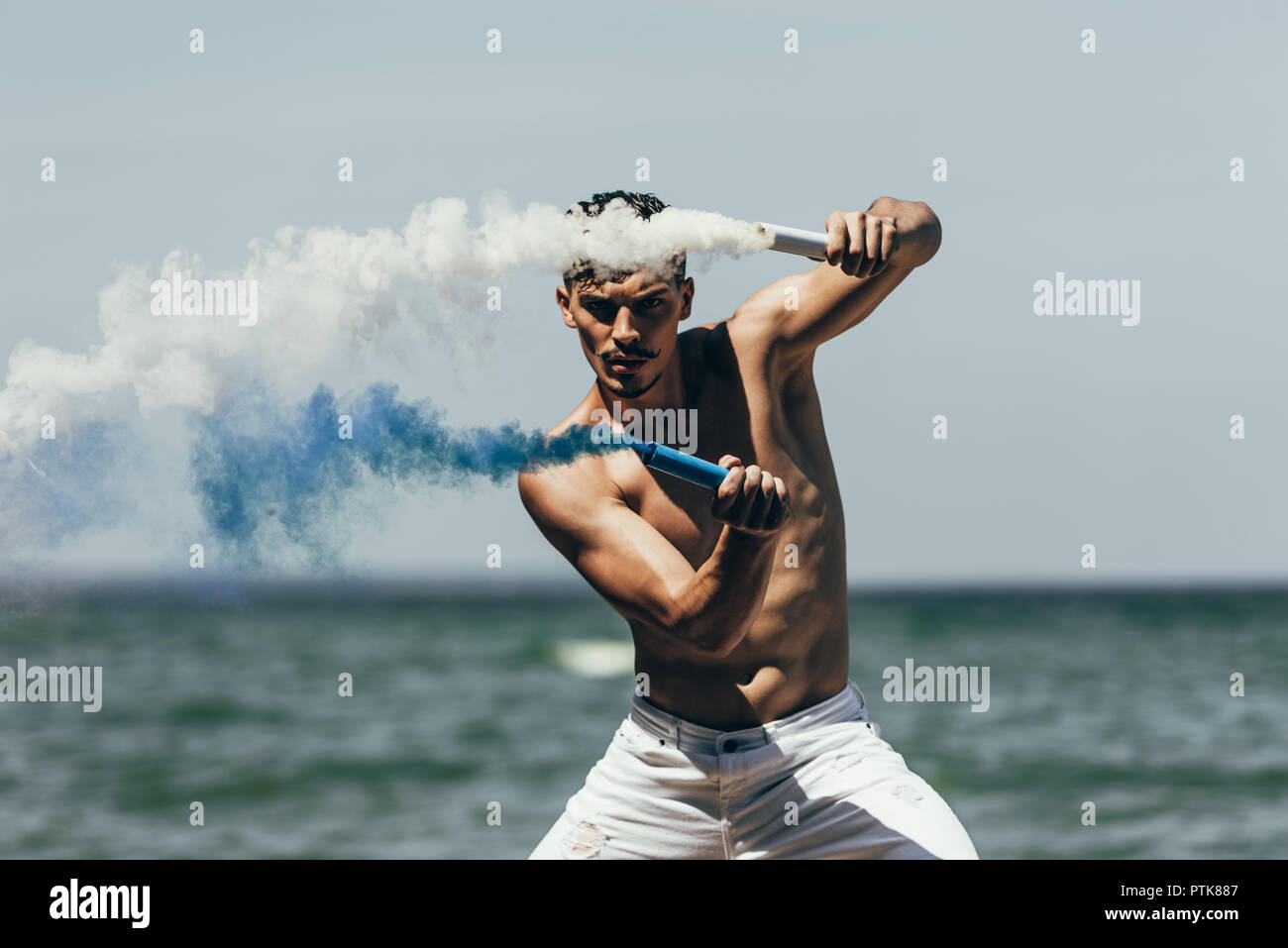 muscular shirtless man dancing with blue and white smoke sticks in ...