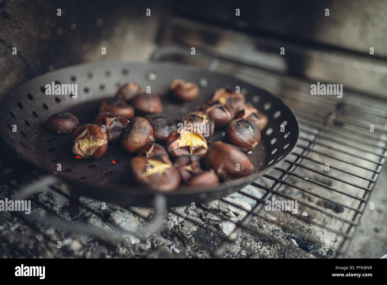 Closeup view of tasty chestnuts roasting on rack above hot embers, with ...