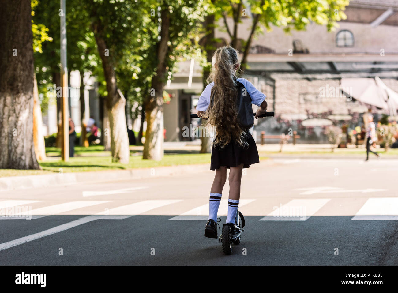 rear view of cute little kid with backpack riding scooter on street ...