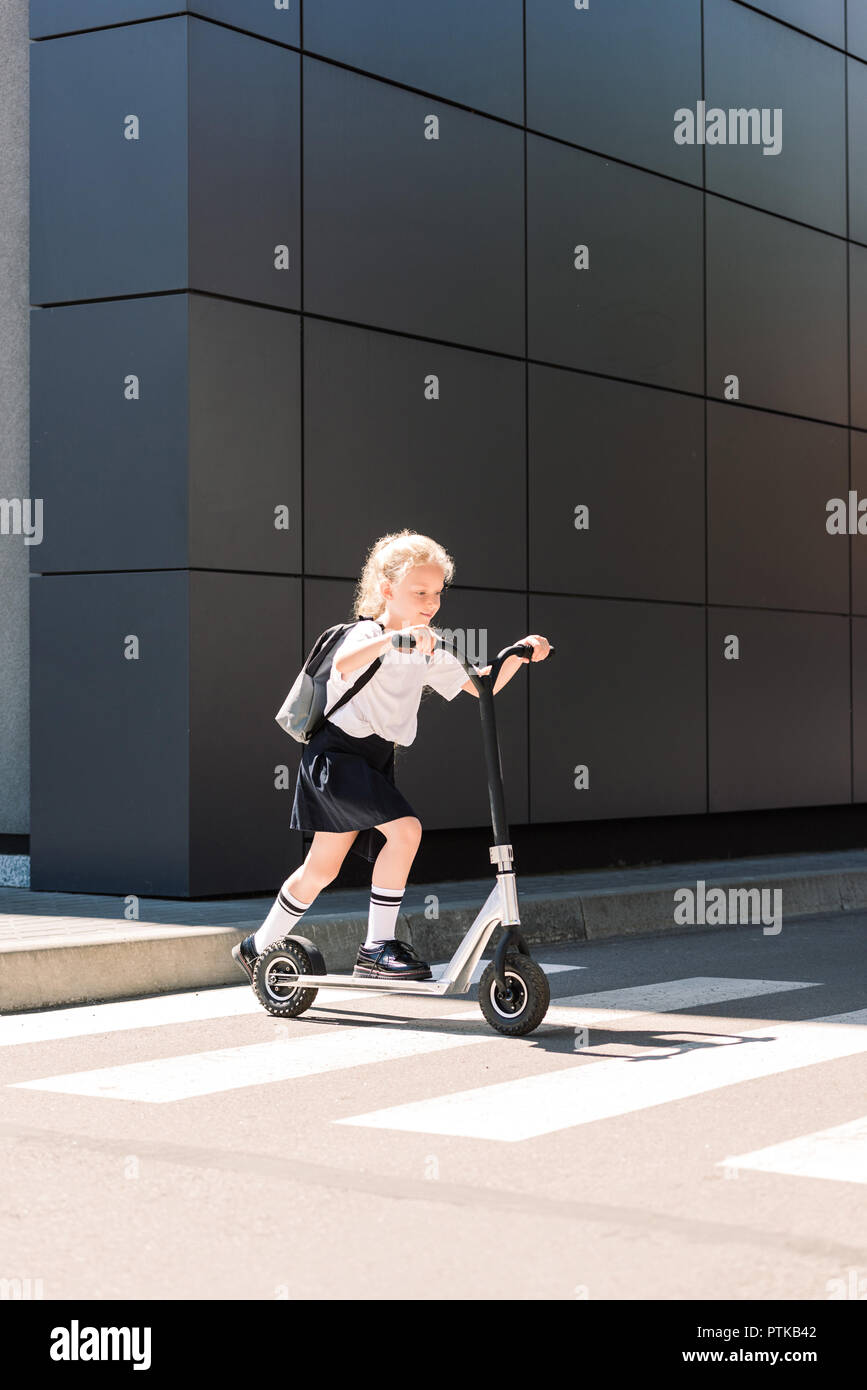 cute little schoolgirl with backpack riding scooter on street Stock ...