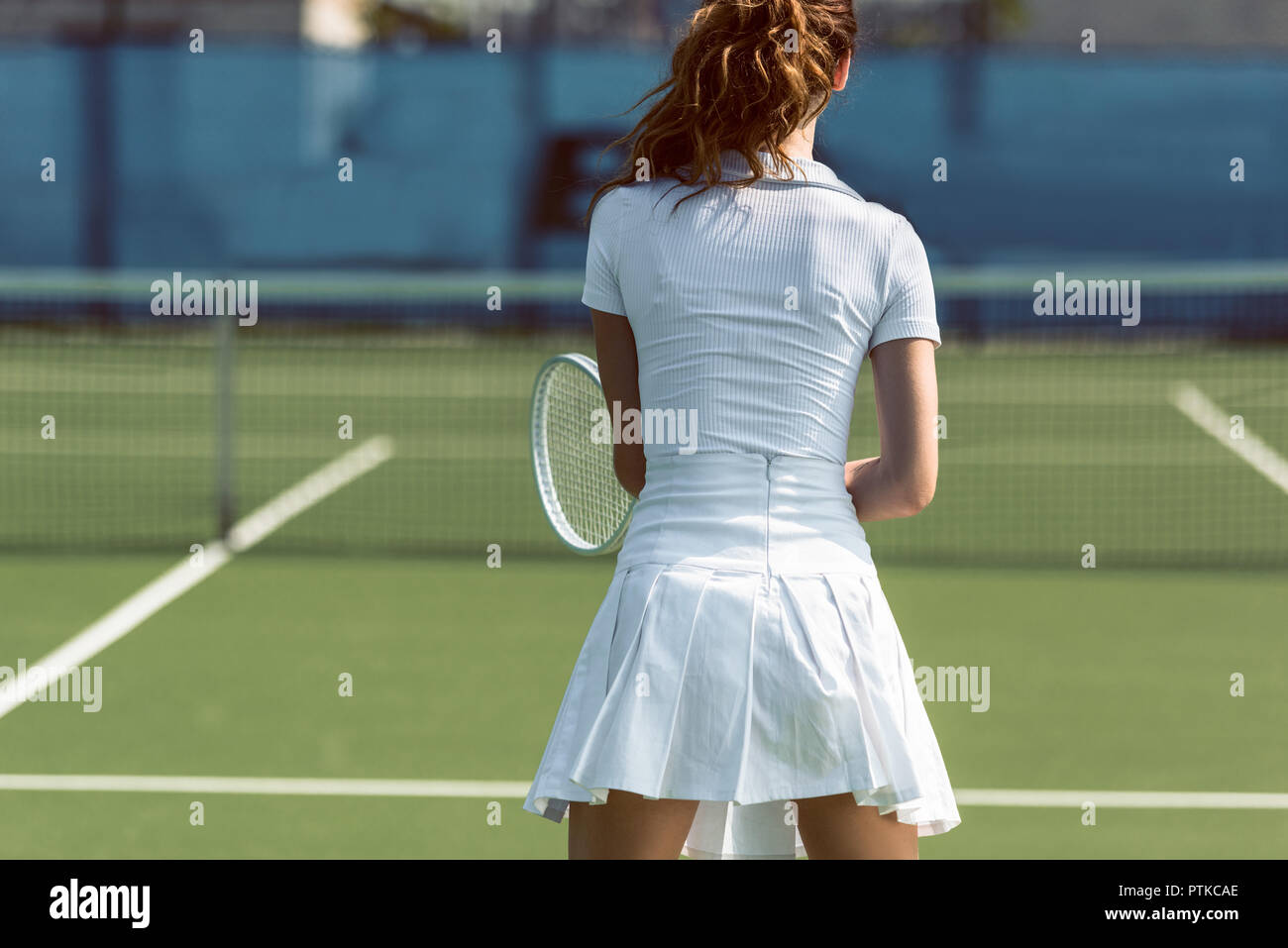 rear view of female tennis player with racket playing tennis on court ...