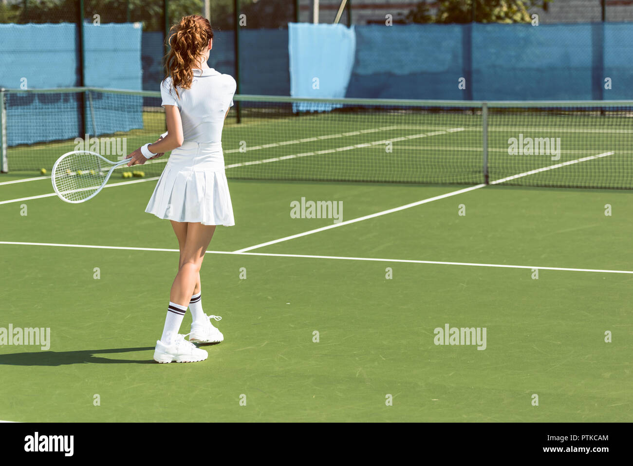 back view of woman in white tennis uniform playing tennis on court ...