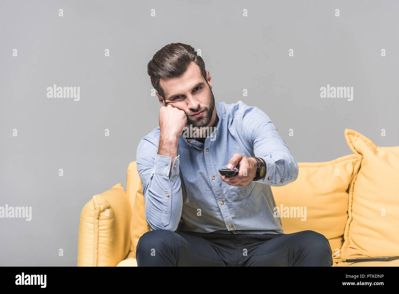 handsome bored man with remote control watching TV on yellow sofa on ...