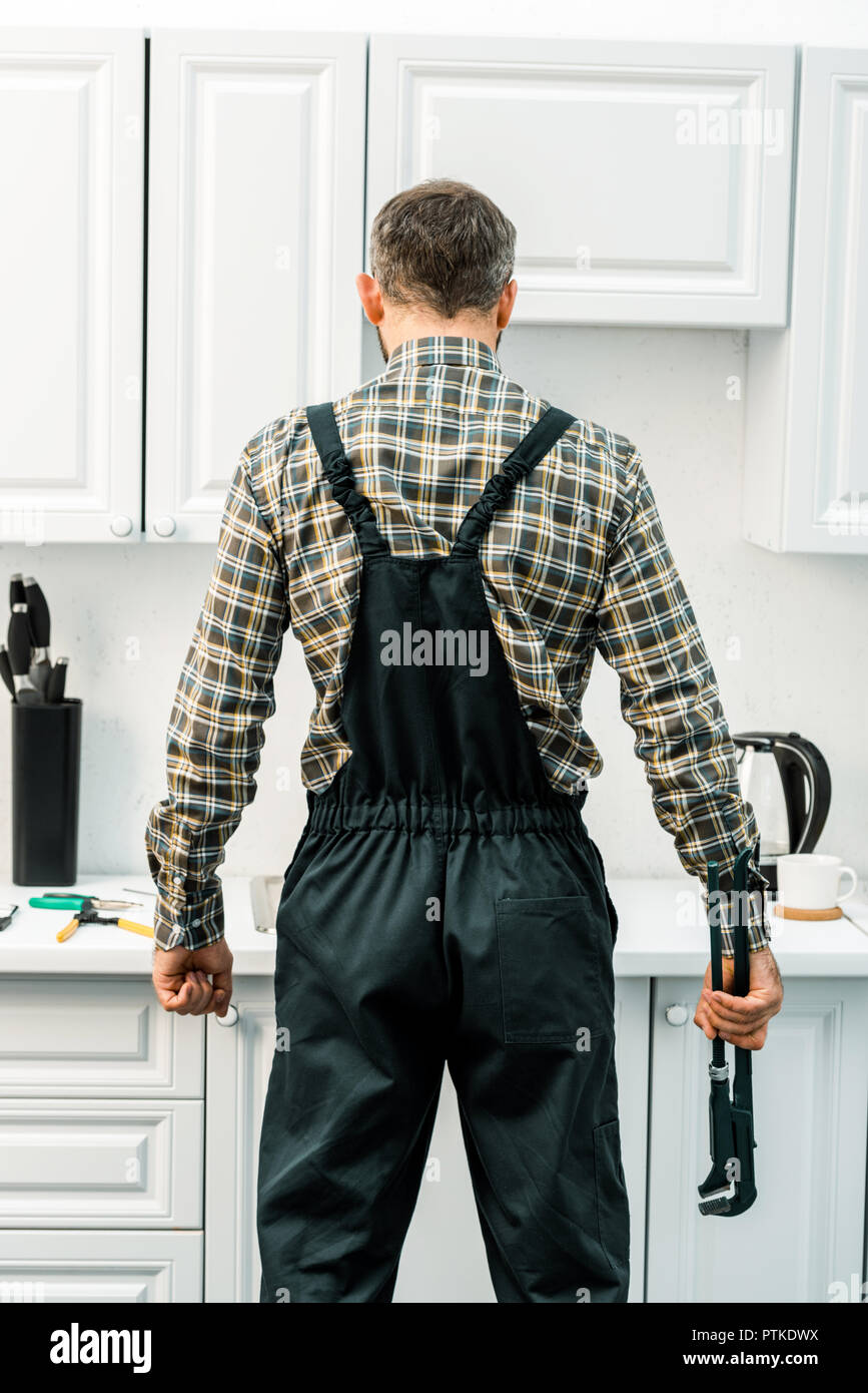 back view of plumber holding monkey wrench and looking at sink in ...