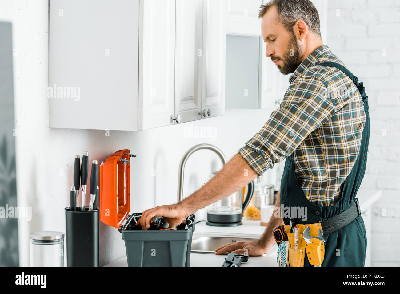 side view of handsome plumber taking tools from toolbox in kitchen ...