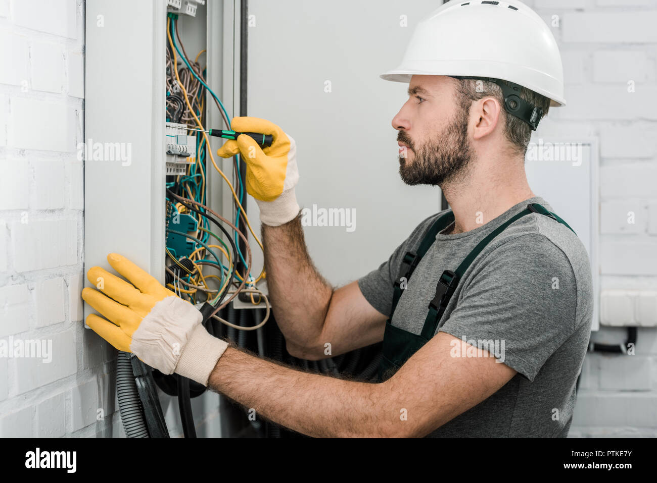 side view of handsome bearded electrician repairing electrical box and ...