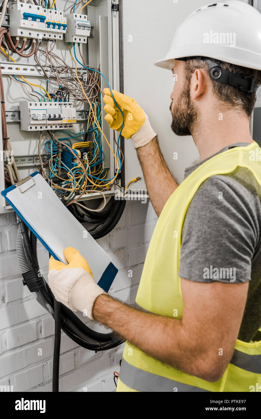 electrician holding clipboard and checking wires in electrical box in ...