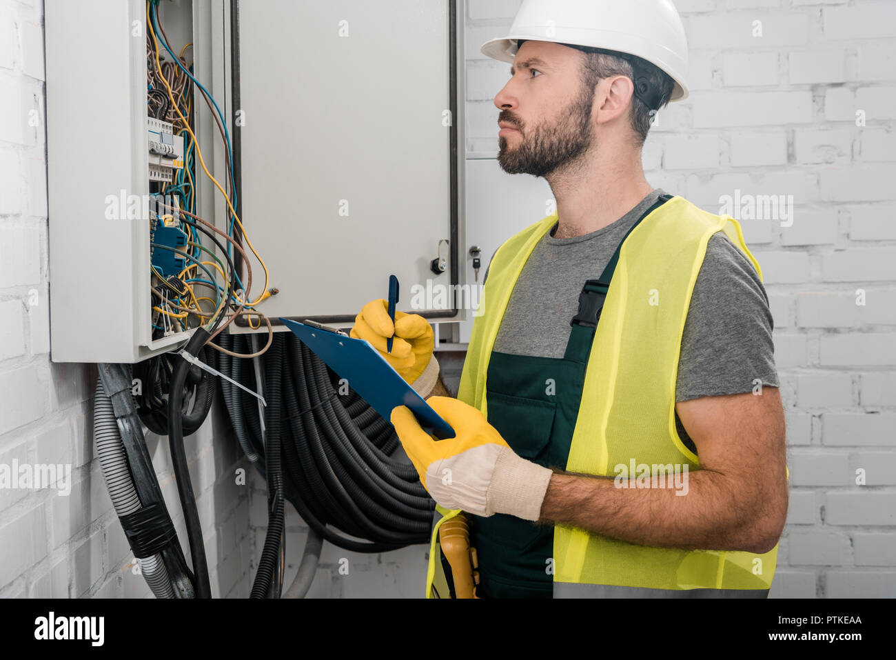 side view of serious electrician holding clipboard and checking ...