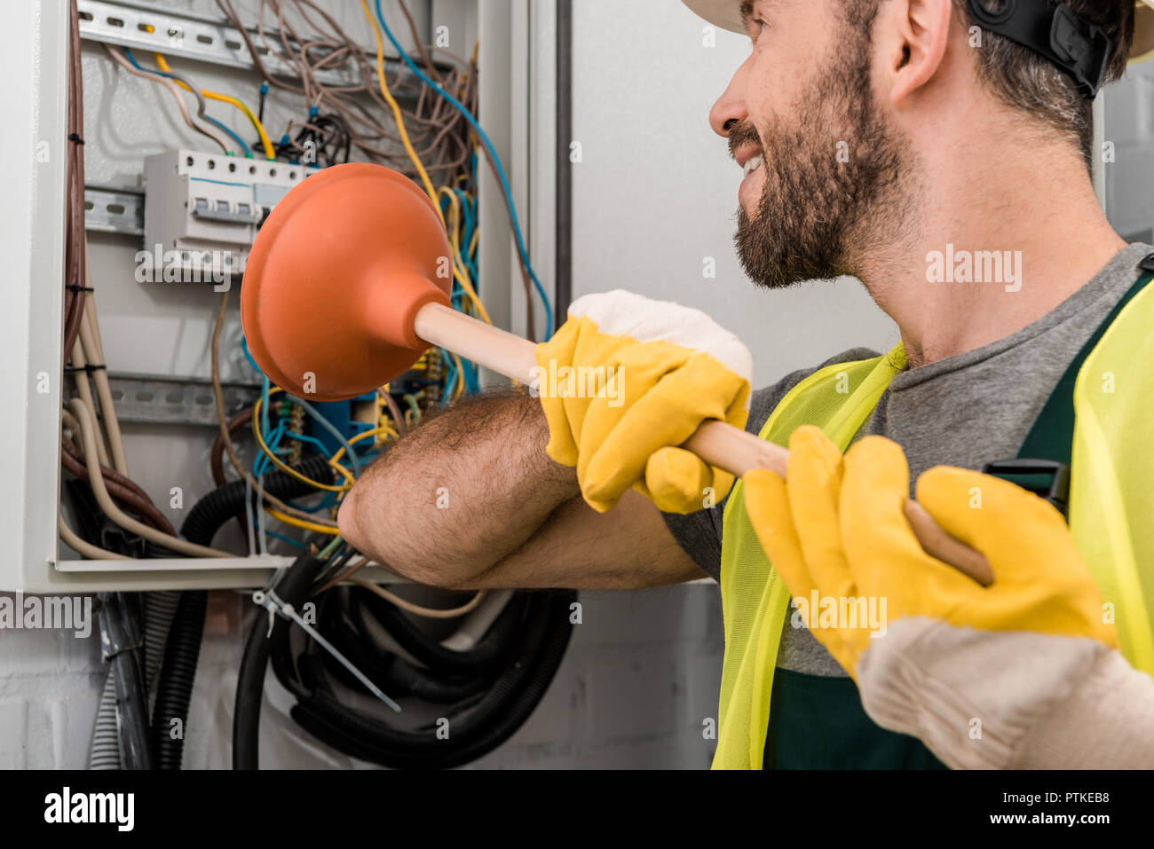 smiling electrician repairing electrical box with plunger in corridor ...