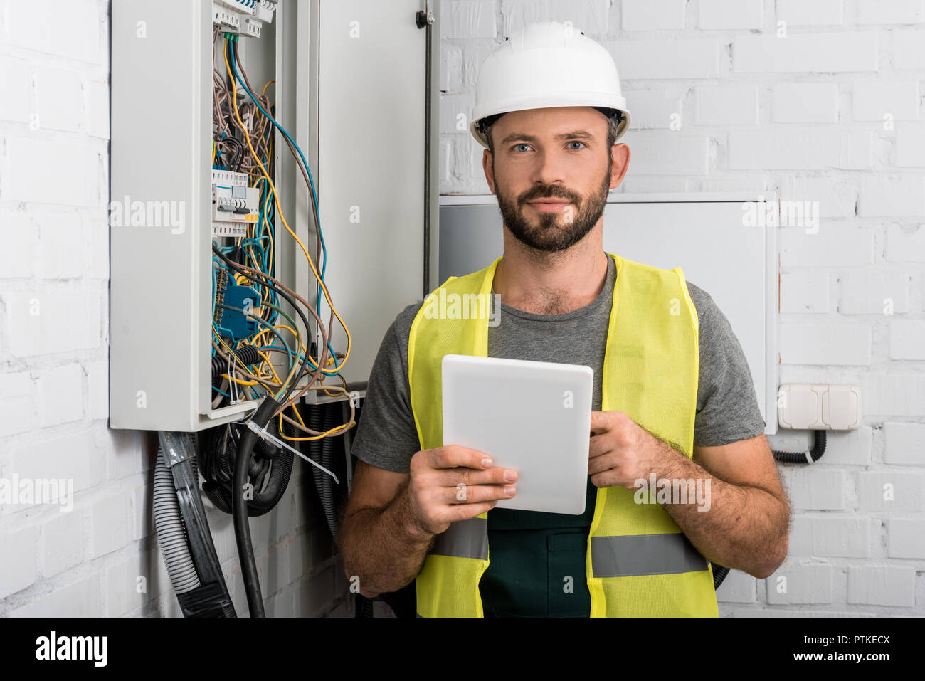 handsome electrician holding tablet near electrical box in corridor and ...