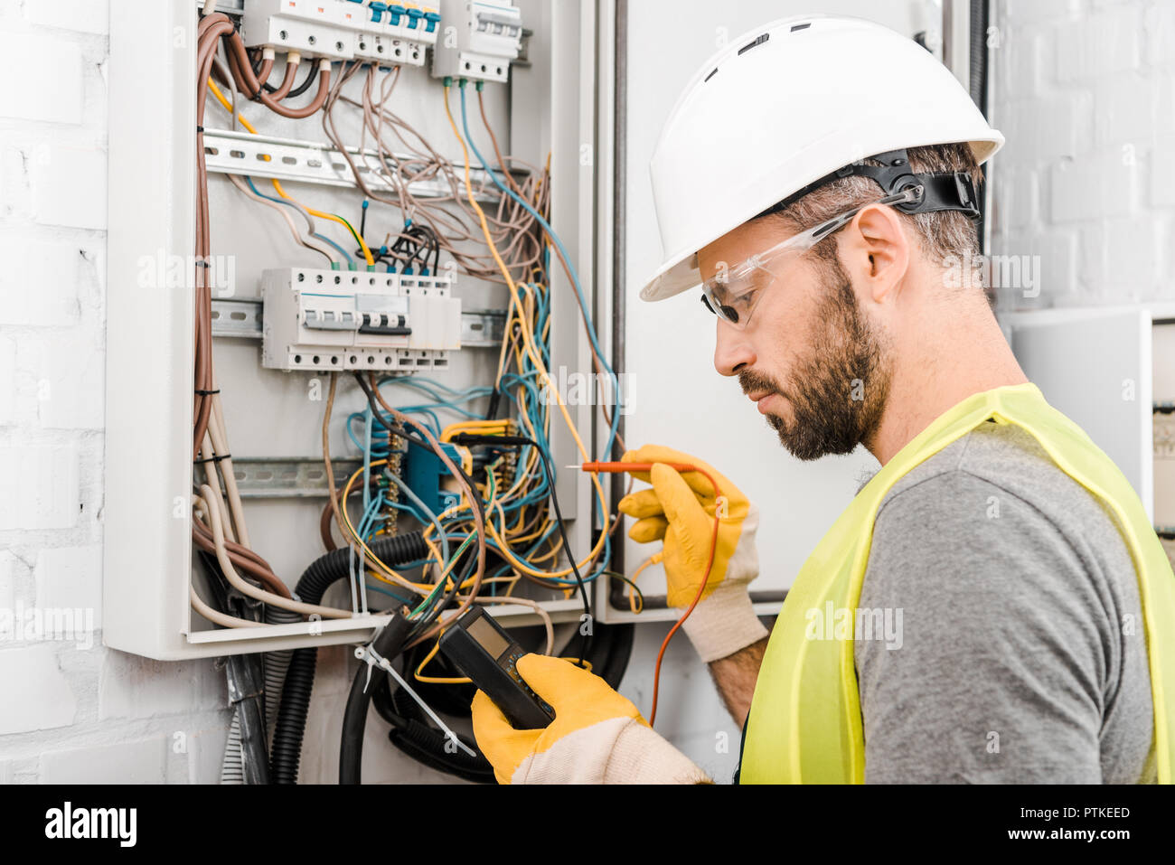 handsome electrician checking electrical box with multimetr in corridor ...