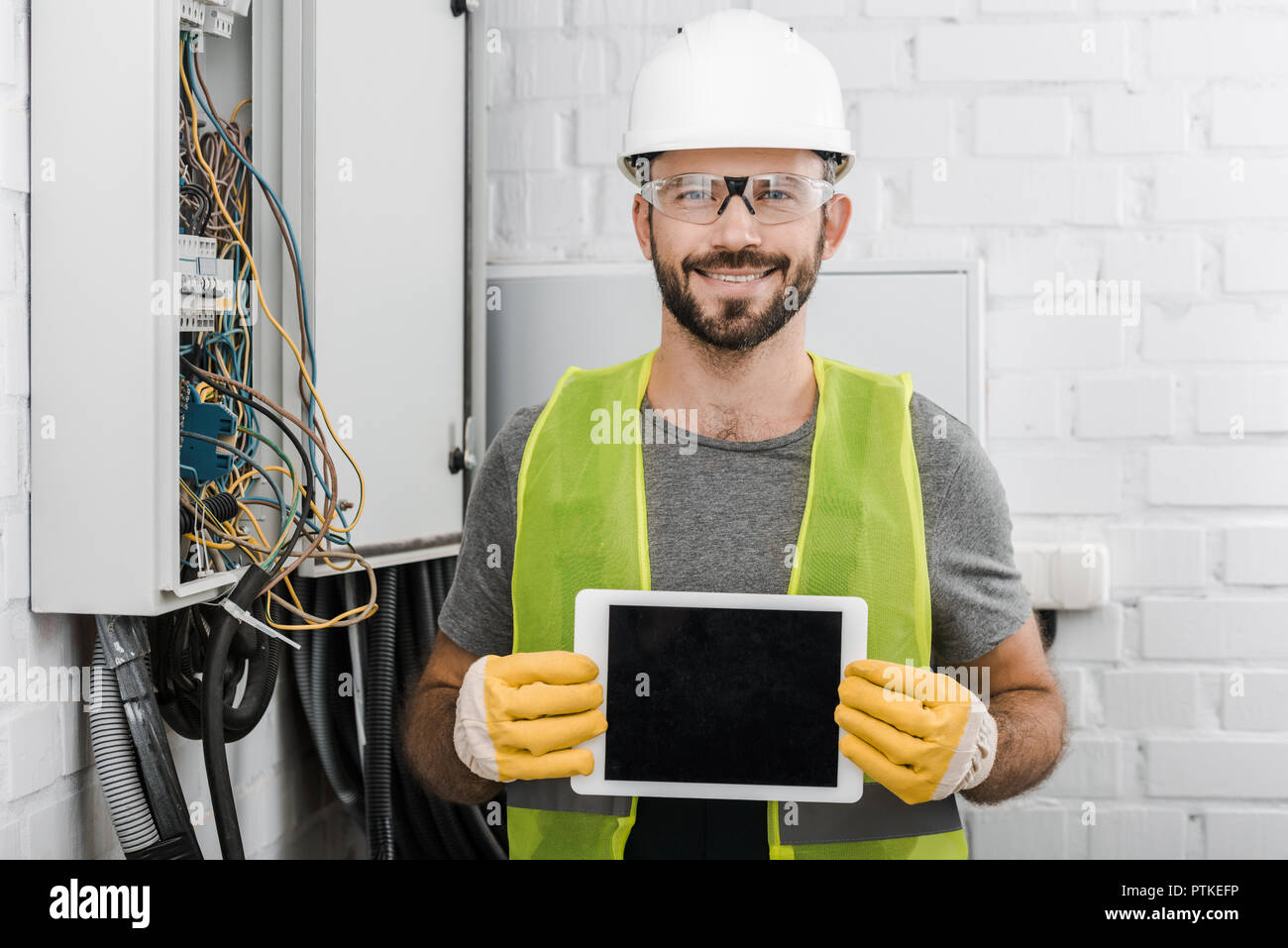 smiling handsome electrician showing tablet with blank screen near ...