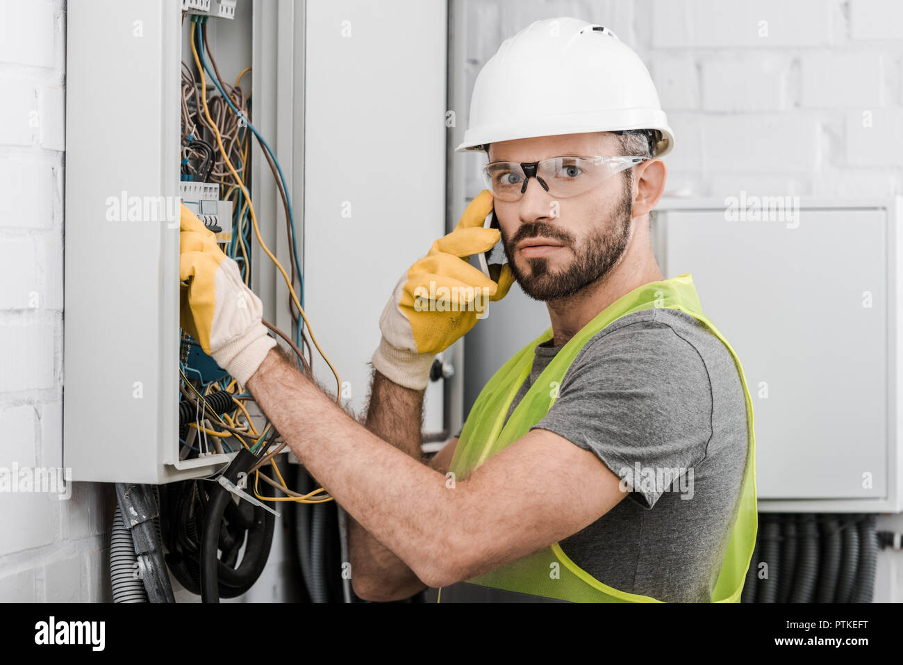 surprised electrician checking electrical box and talking by smartphone ...