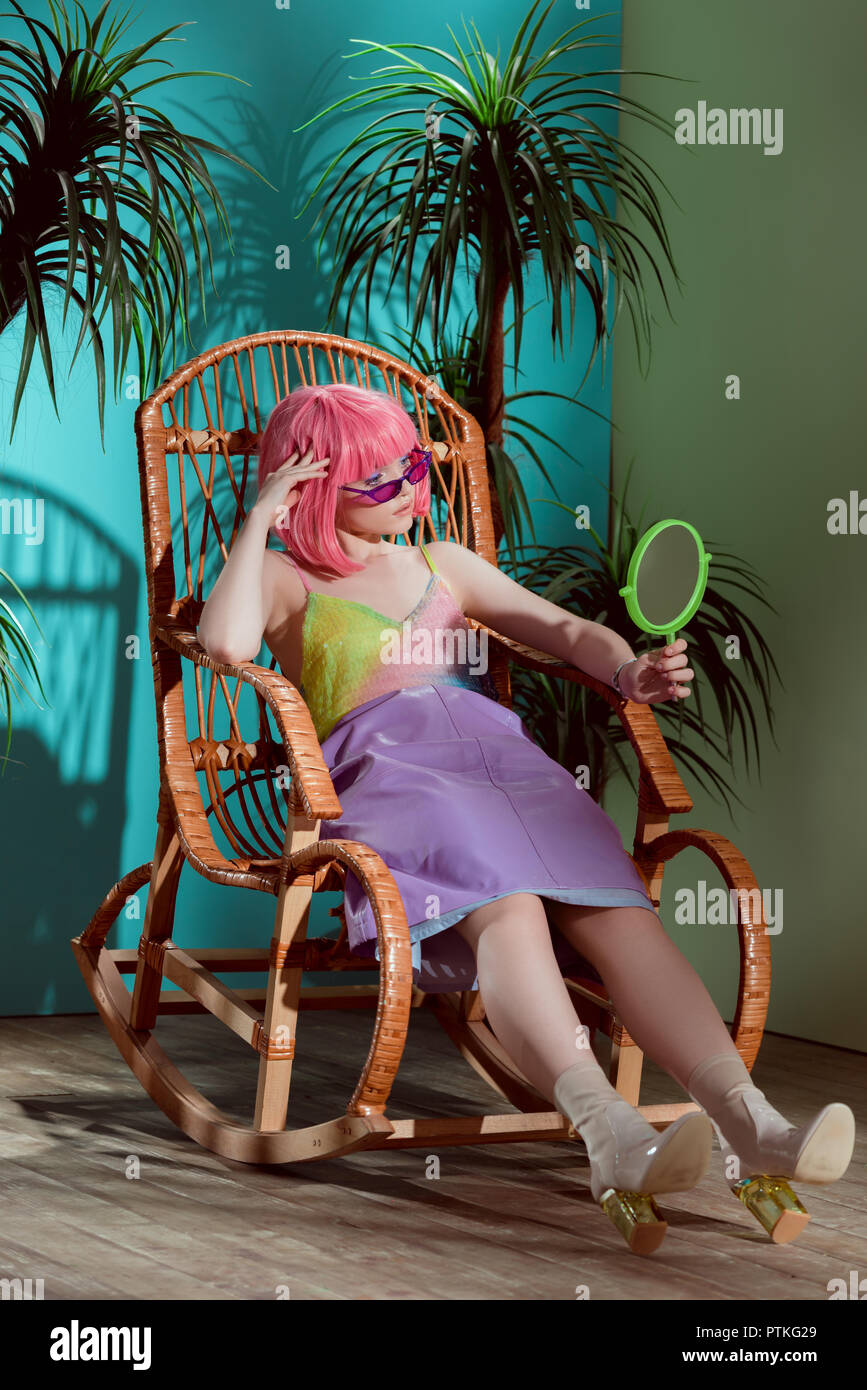 fashionable young female model in pink wig sitting in rocking chair and ...