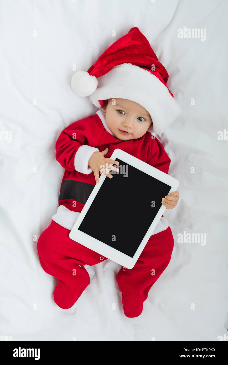 top view of adorable little baby in santa suit lying in crib with ...