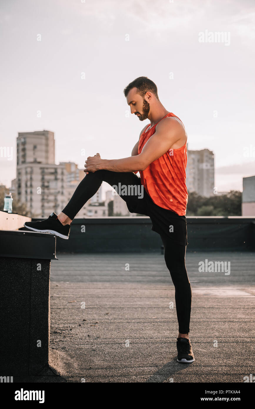 side view of handsome sportsman stretching legs on roof Stock Photo - Alamy