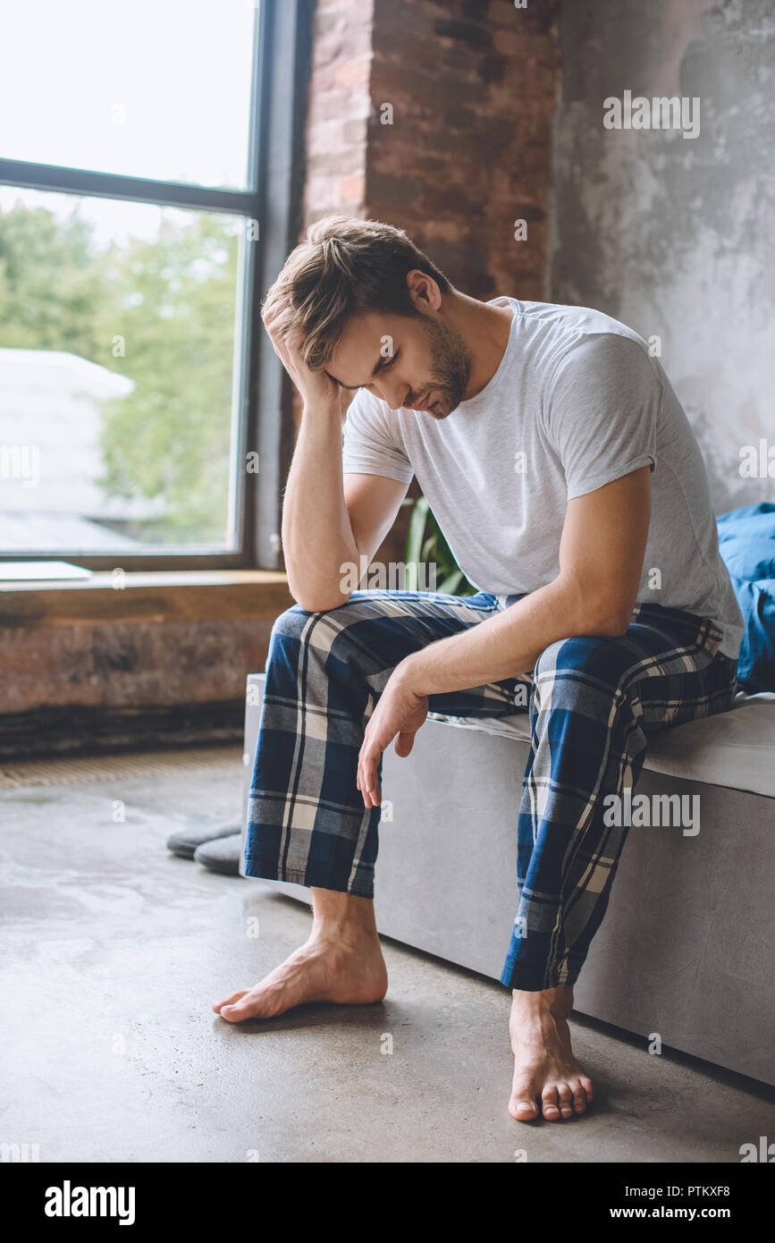 tired young man just wake up and sitting on bed during morning time at ...