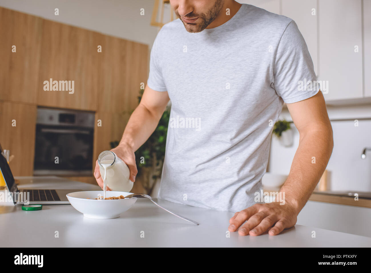 cropped image of man pouring milk into plate with flakes at kitchen ...