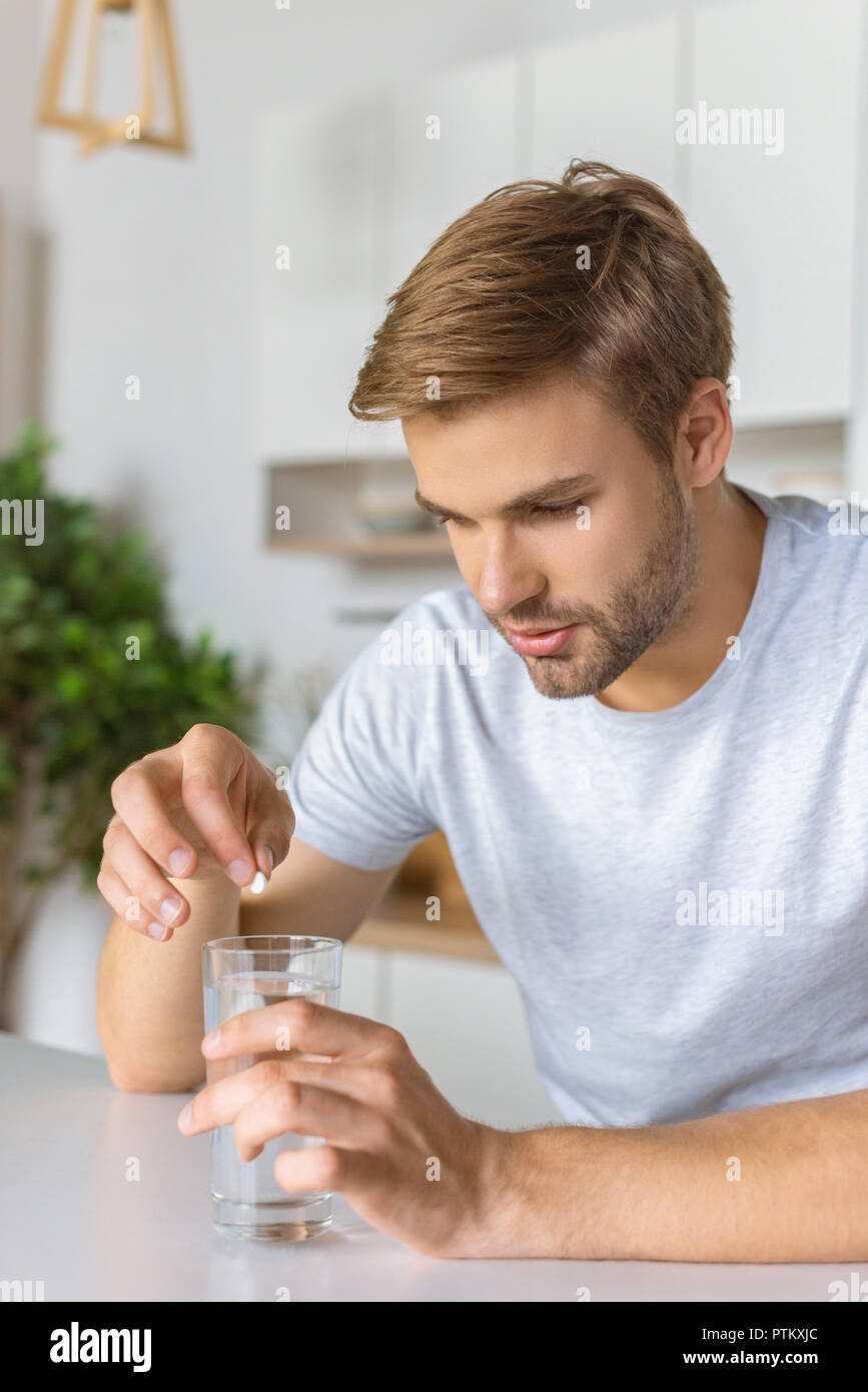young man putting pill into glass with water at kitchen table Stock ...