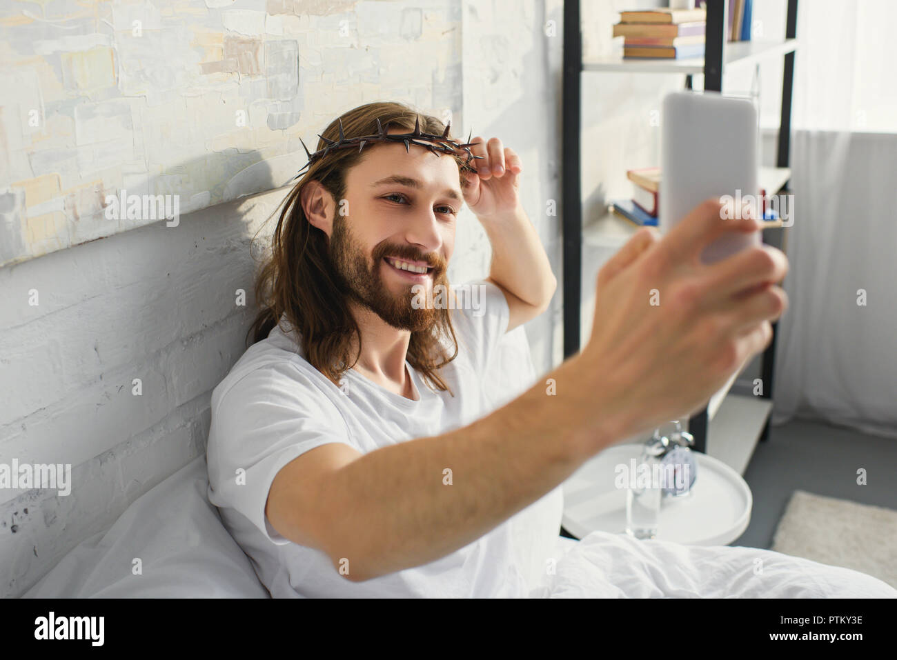high angle view of Jesus in crown of thorns taking selfie in bed during ...