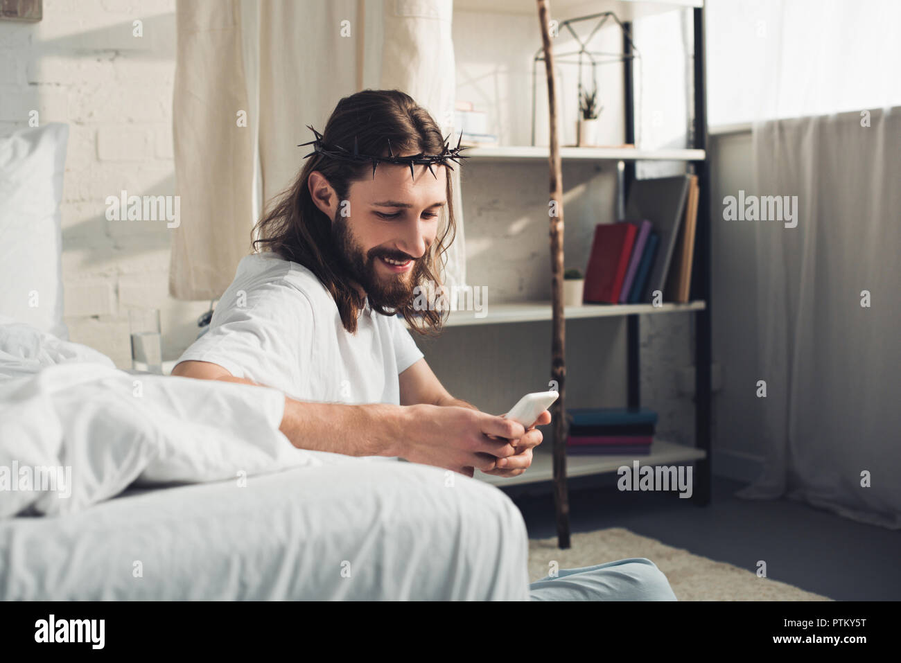 happy Jesus in crown of thorns using smartphone in bedroom at home ...