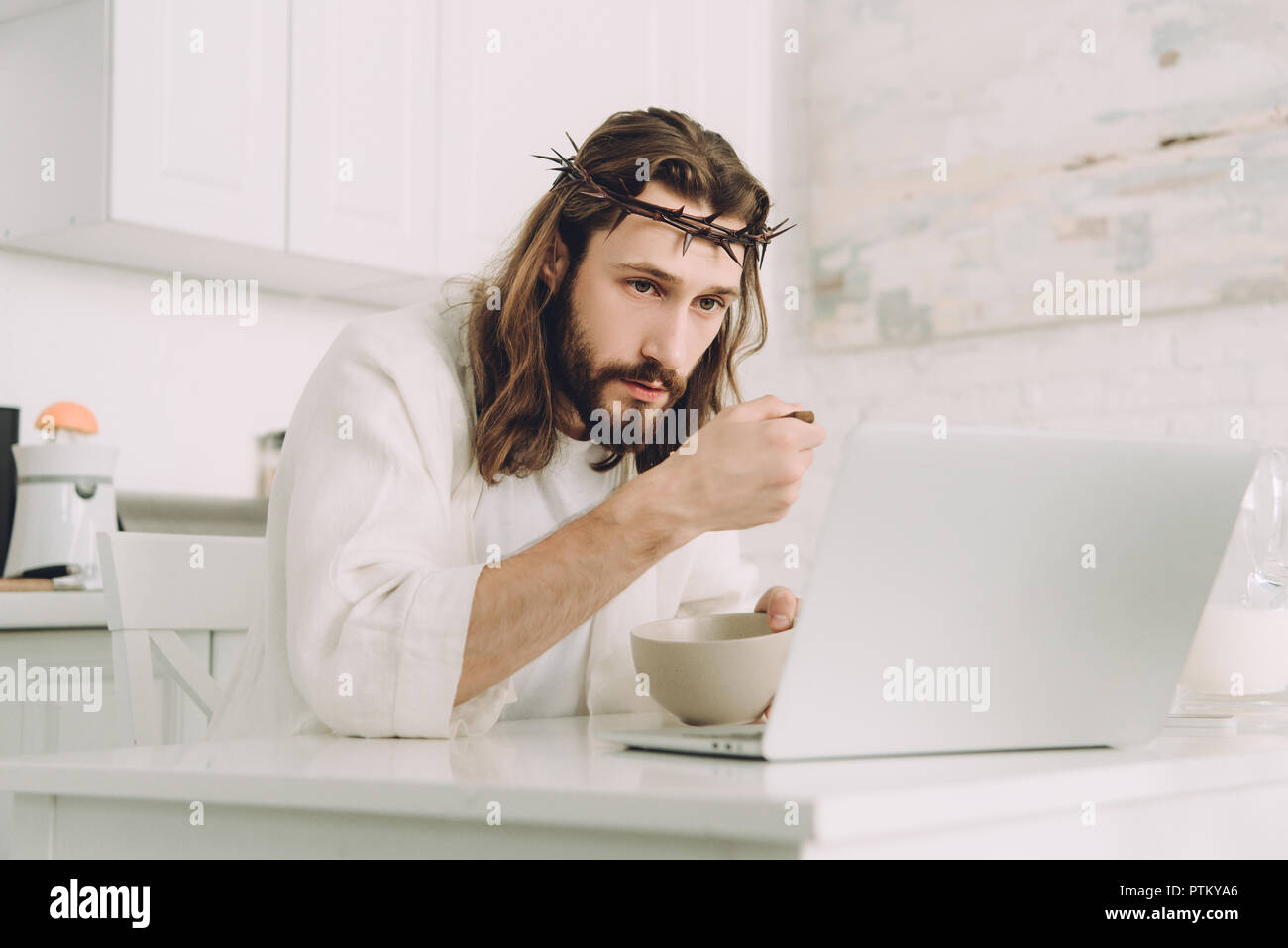focused Jesus eating corn flakes on breakfast at table with laptop in ...