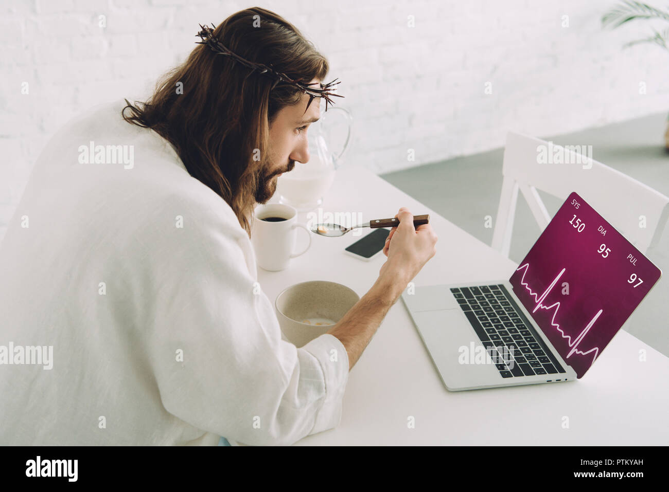 concentrated Jesus eating corn flakes on breakfast at table with laptop ...