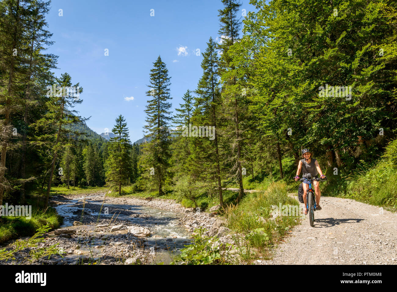 Female cyclist on a cycle path along a stream, crossing the Alps, cycle ...