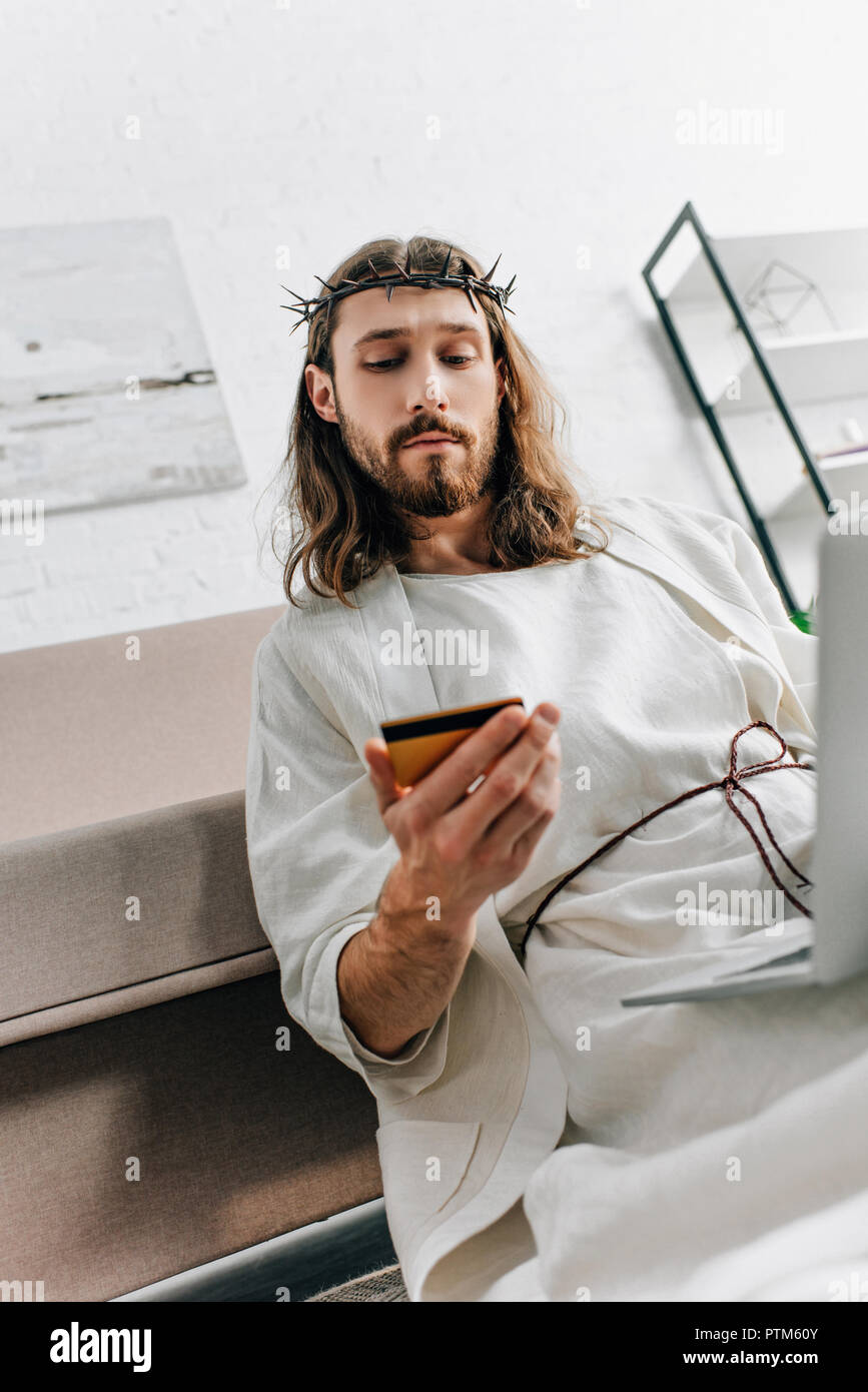 low angle view of pensive Jesus looking at credit card and doing online ...