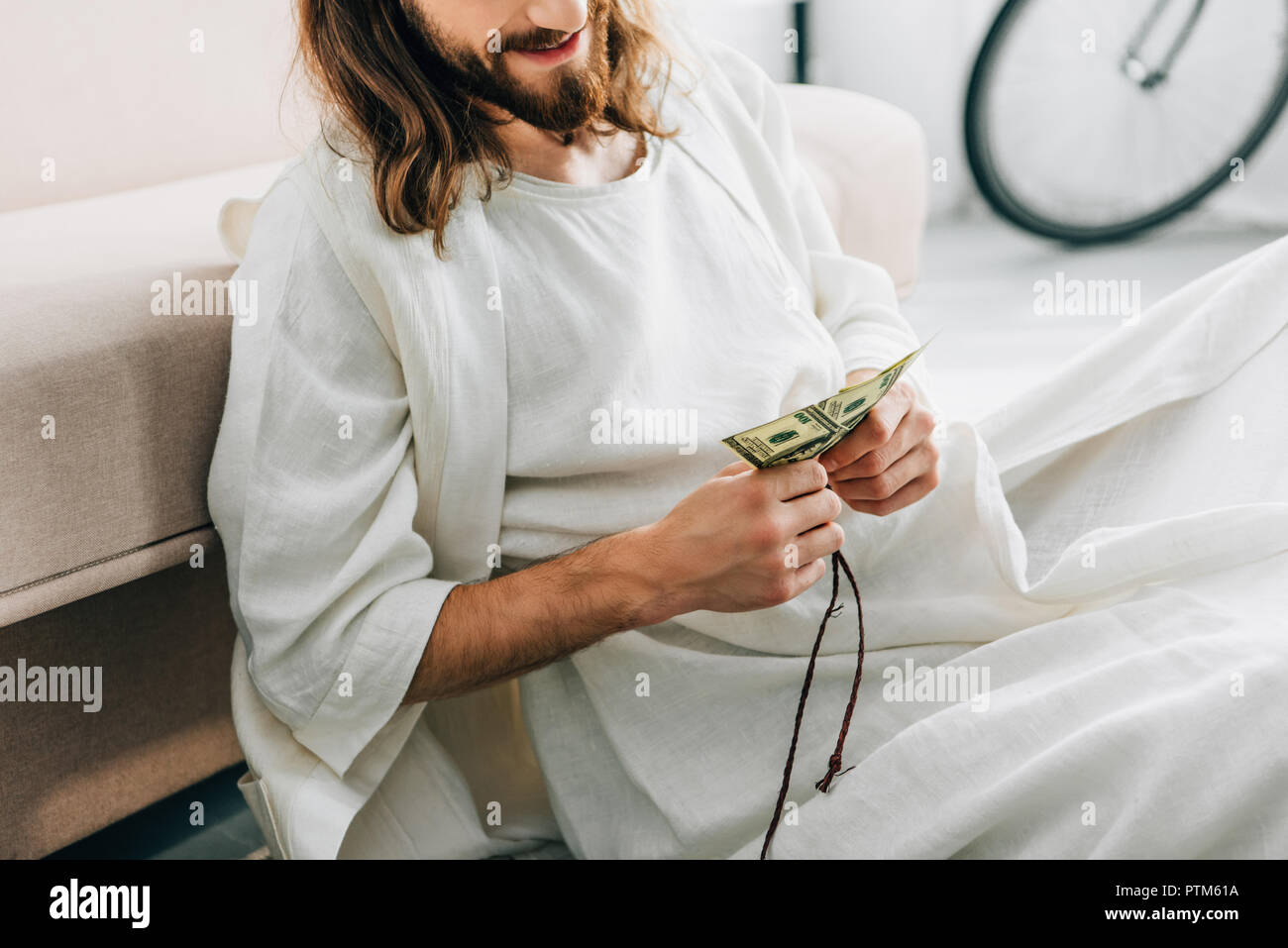 partial view of Jesus sitting on floor near sofa and counting cash at ...
