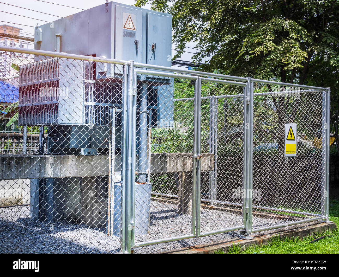 High voltage transformer substation in metal fence with green tree and ...