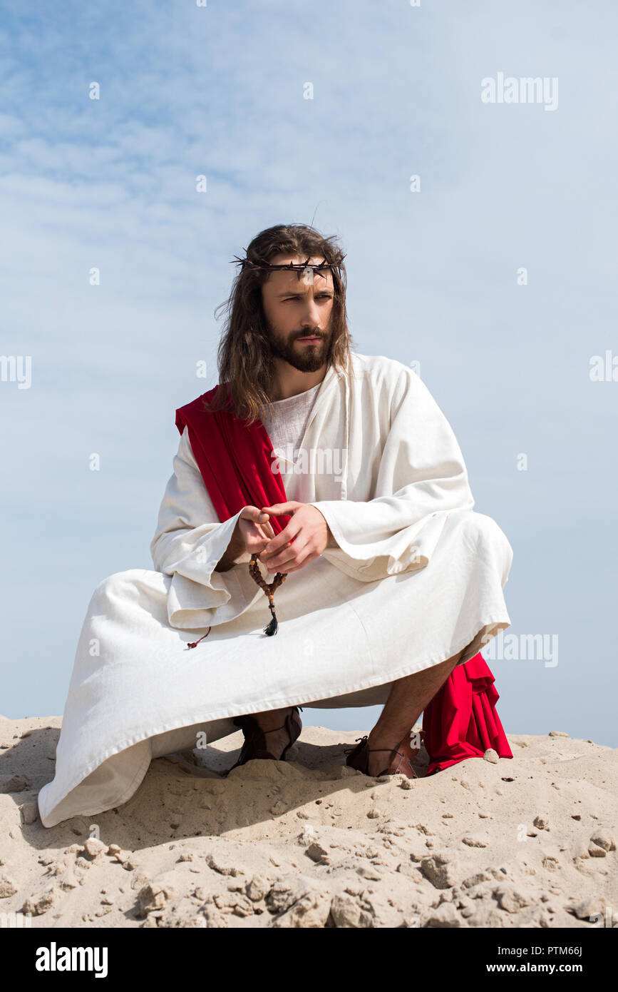 Jesus in robe, red sash and crown of thorns praying with rosary and ...