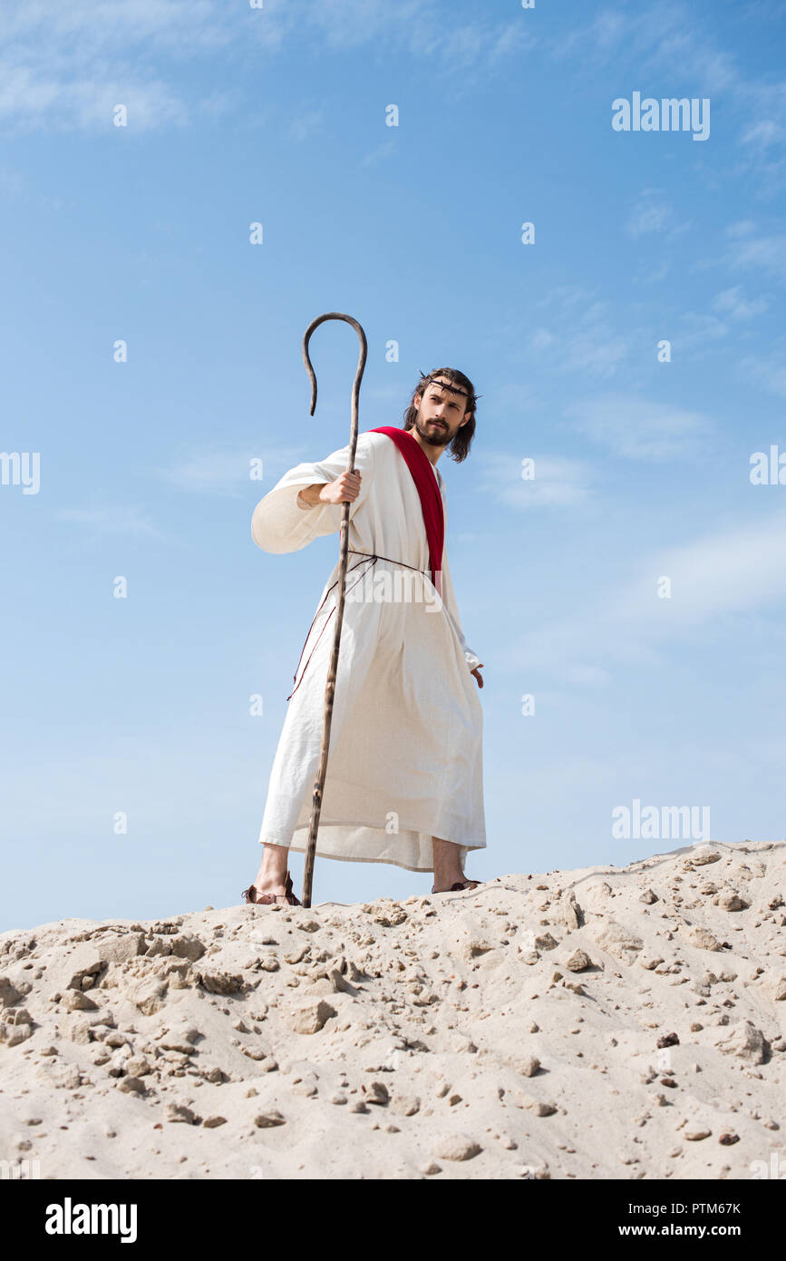 Jesus in robe, red sash and crown of thorns walking on sandy hill with ...