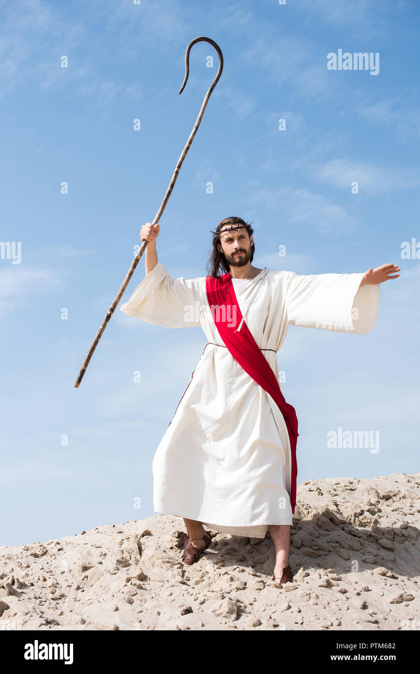 Jesus in robe, red sash and crown of thorns swinging wooden staff in ...