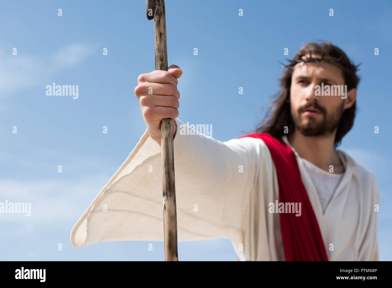 selective focus of Jesus in robe, red sash and crown of thorns holding ...
