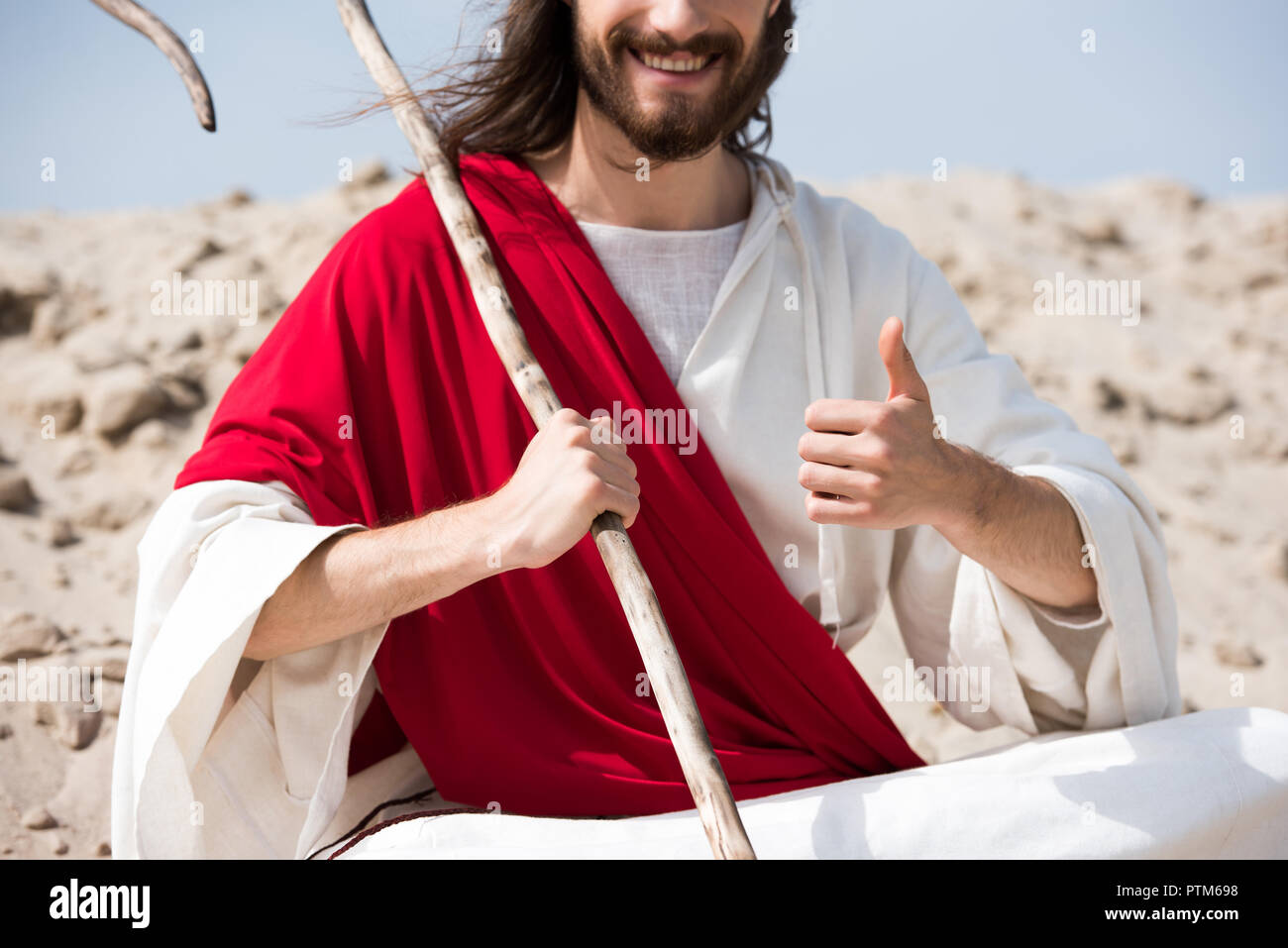 cropped image of Jesus sitting in lotus position on sand, holding staff ...