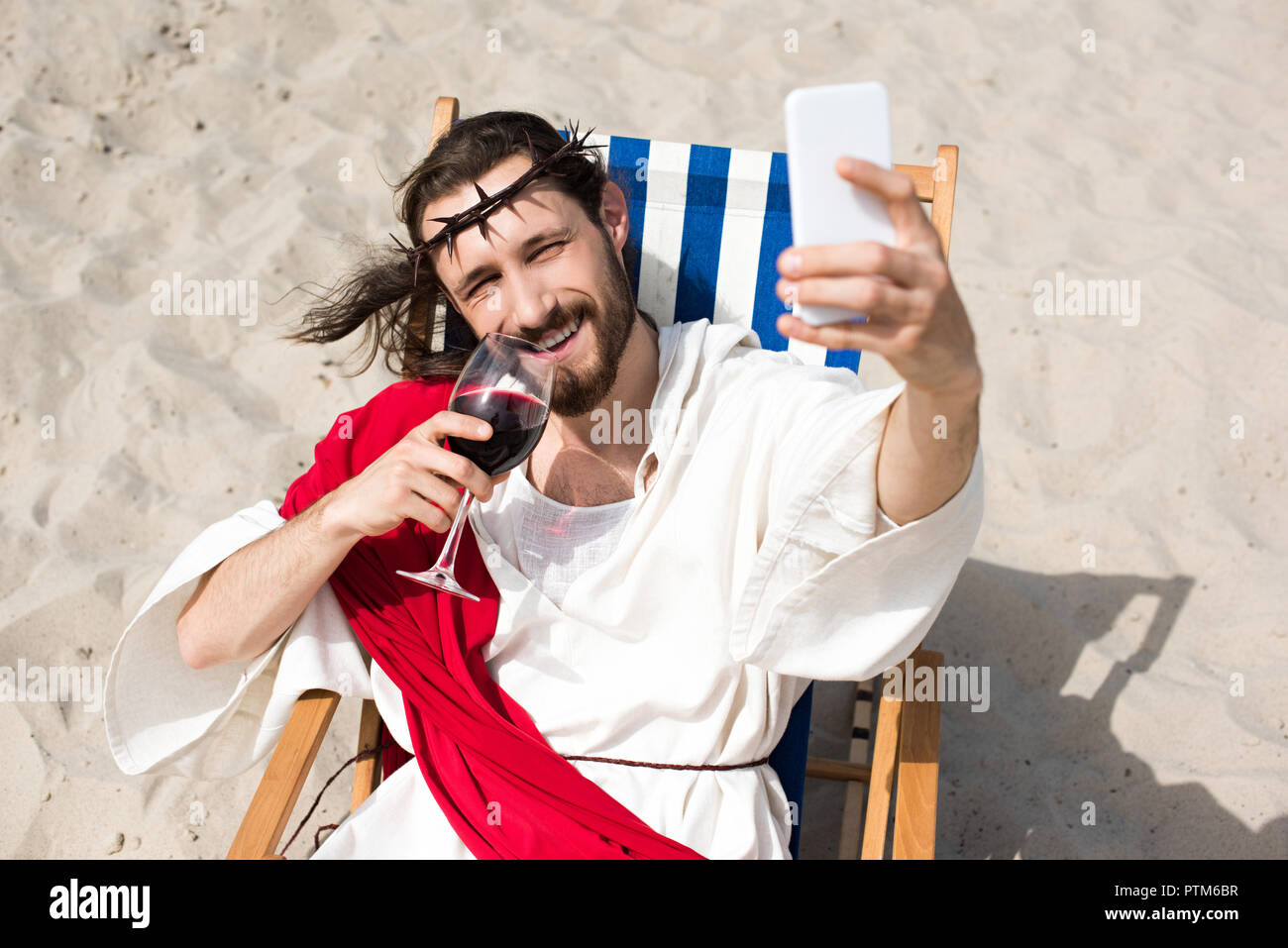 smiling Jesus resting on sun lounger, drinking wine and taking selfie ...