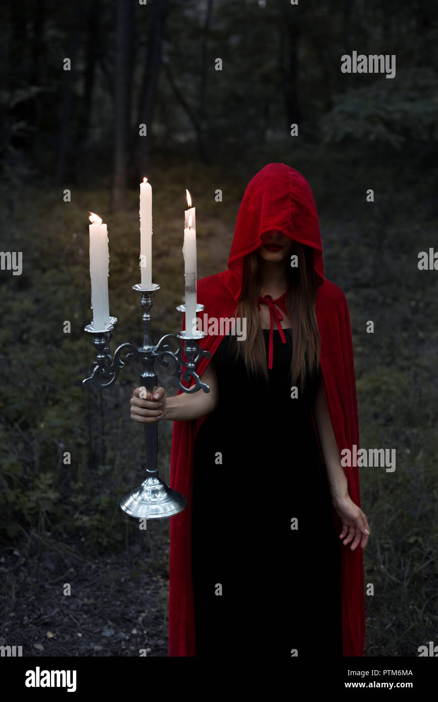 magic woman in red cloak and hood holding candelabrum with candles in ...