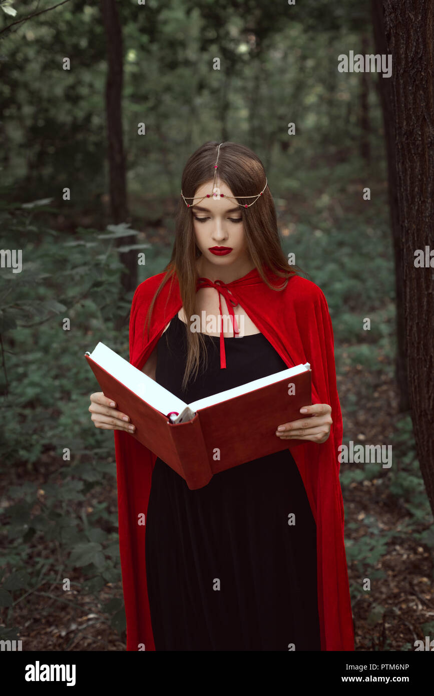 beautiful mystic girl in red cloak and wreath reading magic book in ...