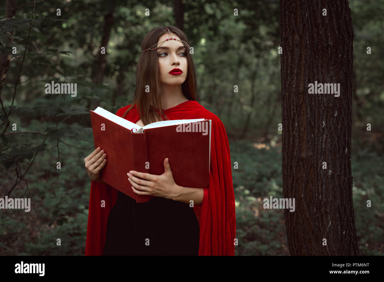 elegant mystic girl in red cloak with magic book in forest Stock Photo ...