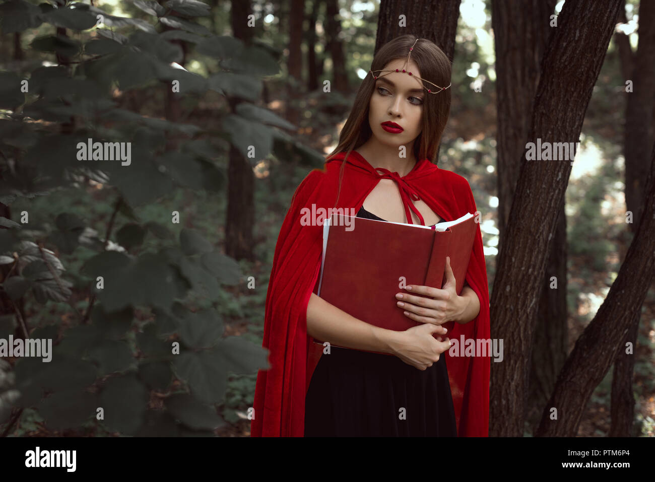 attractive girl in red cloak with magic book in dark woods Stock Photo ...