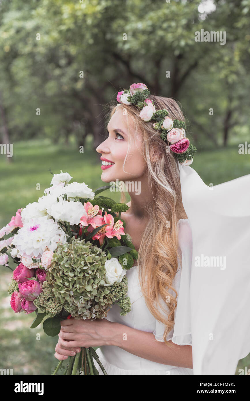 side view of beautiful smiling young bride in veil holding wedding ...