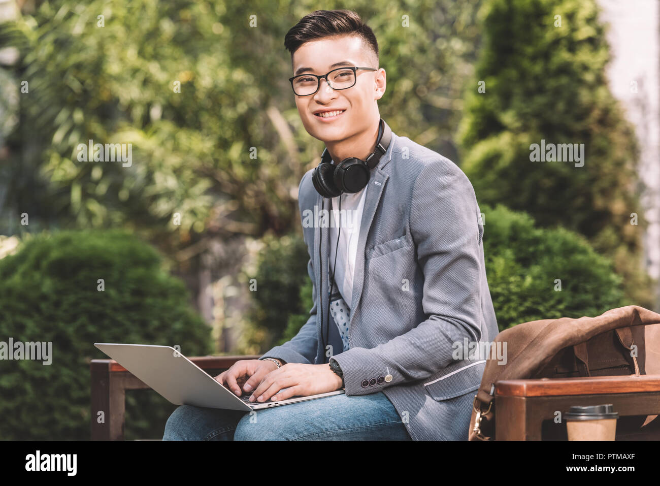 smiling asian freelancer working on laptop while sitting on bench Stock ...