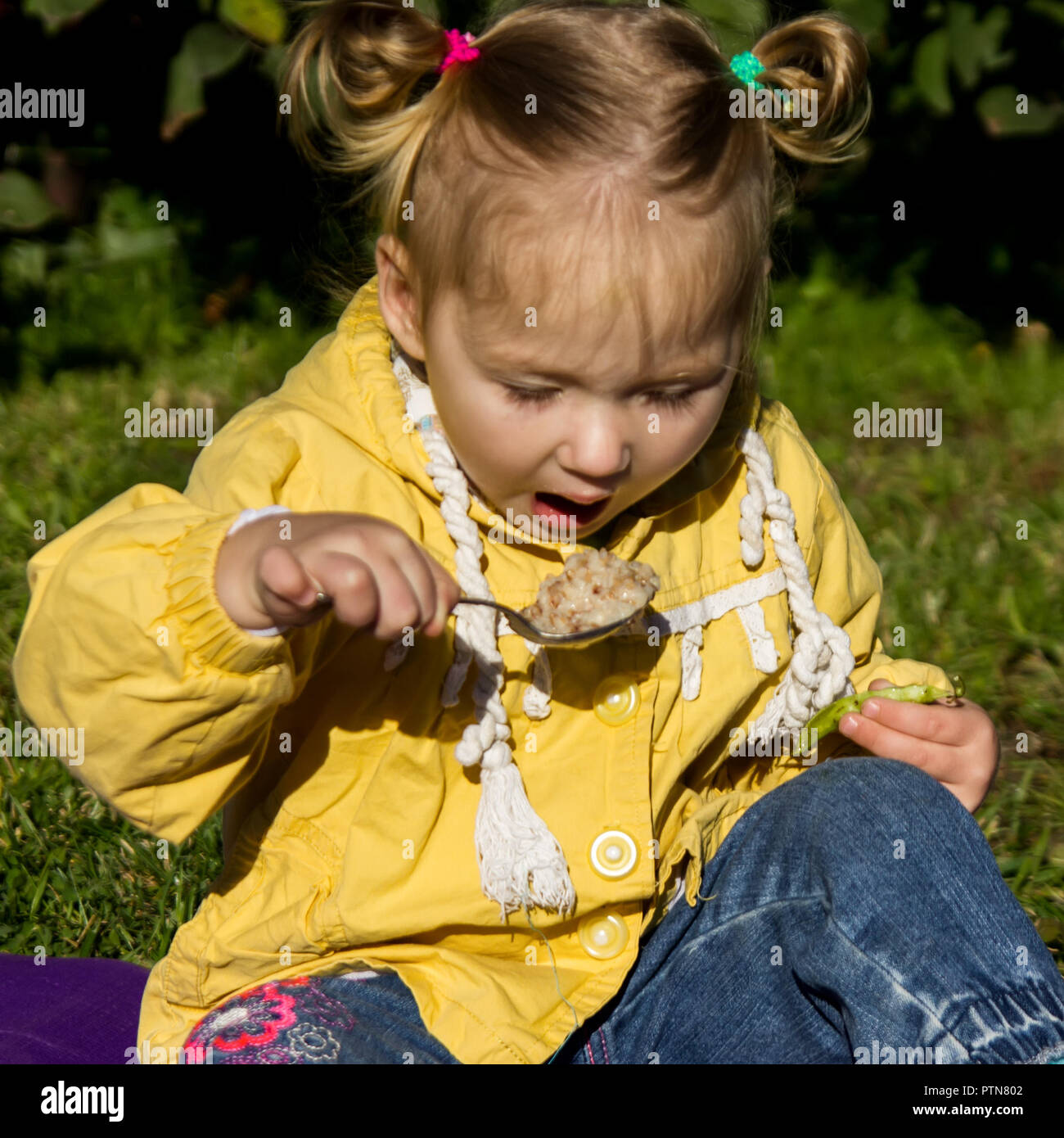 little girl is sitting on a grass and eating porridge Stock Photo - Alamy