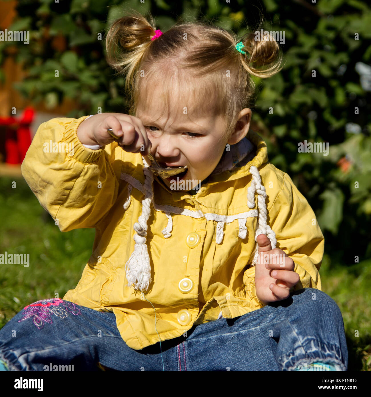 little girl is sitting on a grass and eating porridge Stock Photo - Alamy