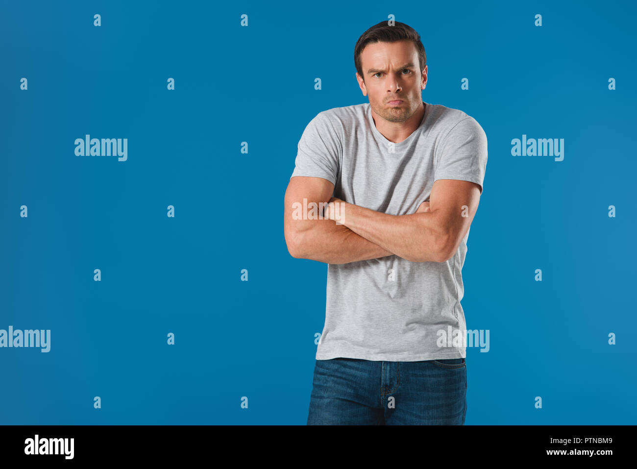 frowning man standing with crossed arms and looking at camera isolated ...