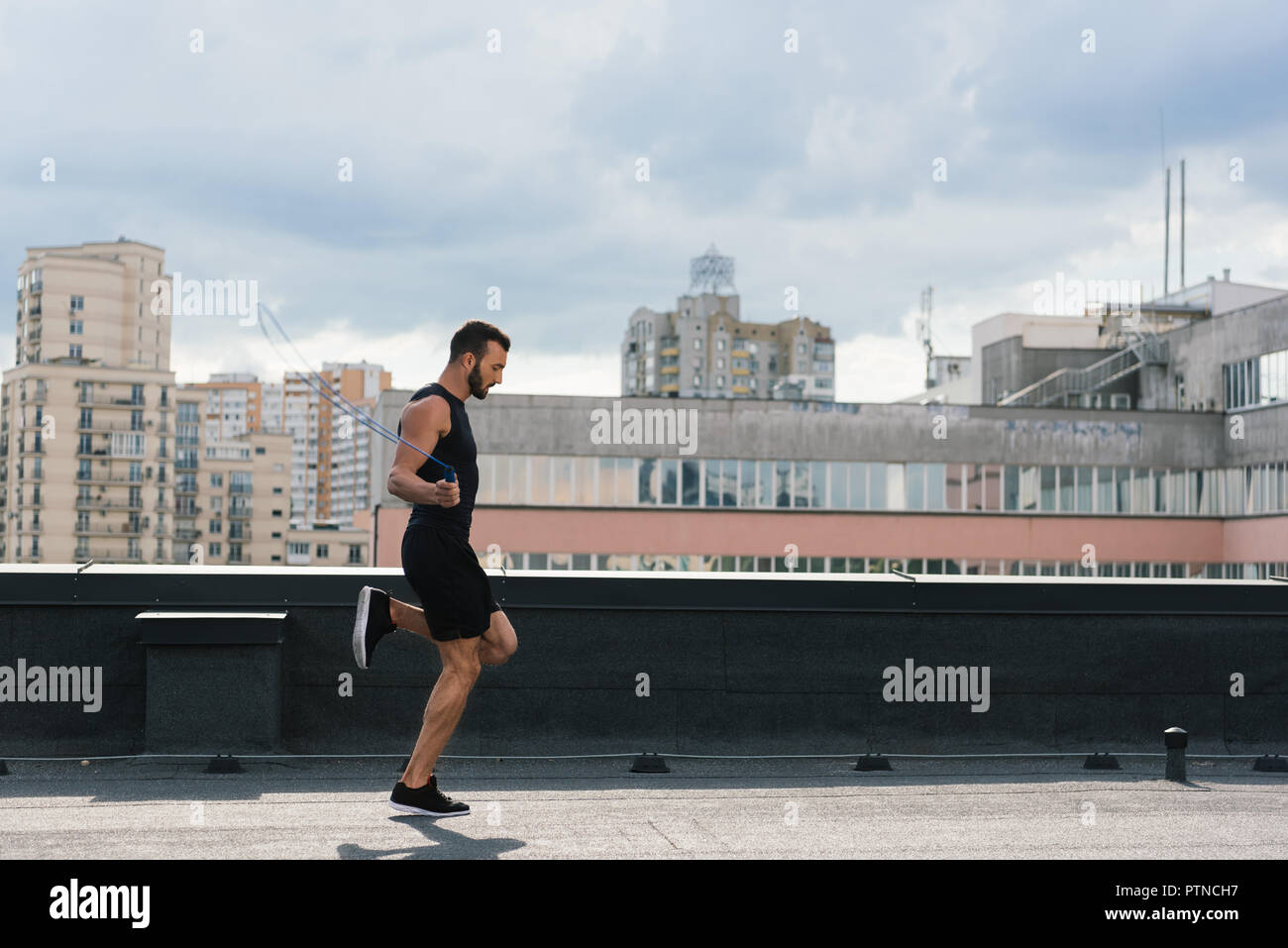 side view of handsome sportsman jumping with jumping rope on roof Stock ...