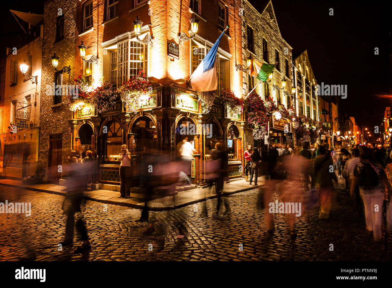 Busy nighttime street scene with blurred people around The Quays Bar ...