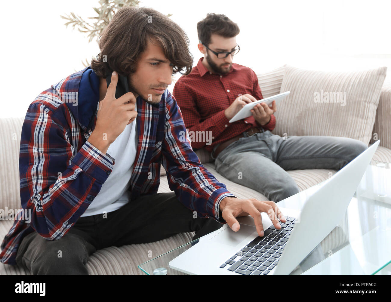 two guys sitting on the couch, talking on the smartphone and ...